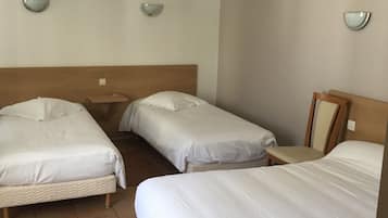 Quarto de hotel com três camas de solteiro, cabeceira de madeira, mesa de cabeceira e luminárias fixadas na parede.