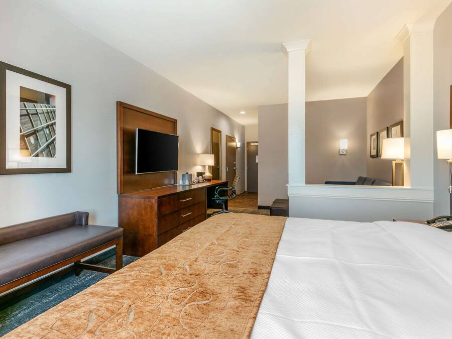 Quarto de hotel com uma cama grande, uma escrivaninha com televisão de tela plana, um banco, uma cômoda e um espelho.