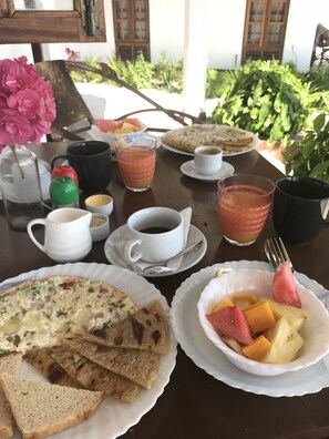 Uma mesa de café da manhã com diversos pratos, incluindo torradas, uma saladeira de frutas e um prato de comida, além de xícaras e um copo de suco.