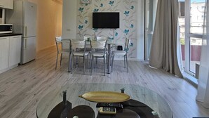 Uma cozinha moderna com micro-ondas e frigorífico embutidos, área de jantar com mesa e cadeiras de vidro, e uma janela grande com cortinas.