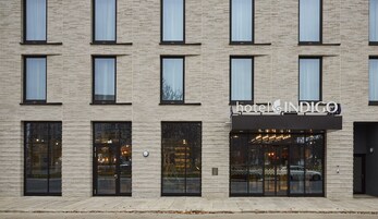 Um hotel com fachada moderna de tijolos, janelas amplas e um letreiro chamativo 'hotel INDIGO'.