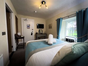 Quarto de hotel com cama, televisão, secretária com computador, janela com cortinas e porta com placa de proibido fumar.