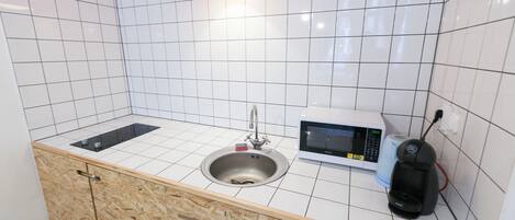 Uma pequena cozinha compacta com pia, micro-ondas e aquecedor portátil.