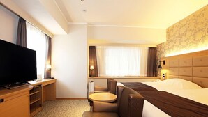 Quarto de hotel com cama, televisão, pequena mesa, sofá e janela com cortinas.