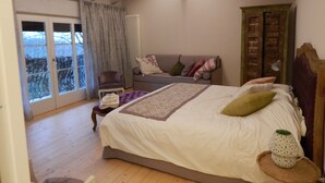 Quarto com uma cama grande, uma cadeira, um sofá, um armário de madeira e vista para o exterior.