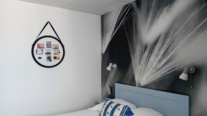 Quarto com cama, luminária na parede e uma obra de arte na parede.