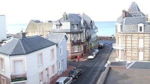 Uma rua costeira com edifícios, incluindo uma casa em estilo Tudor e uma construção de tijolos, que leva ao mar.