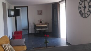 Uma sala de estar moderna com sofá, televisão de tela plana, área de jantar com mesa e cadeiras, e um relógio de parede grande.