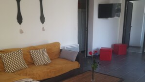 Uma sala de estar moderna com um sofá, um banquinho estampado, uma mesa de centro e uma televisão de tela plana na parede.