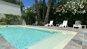 Piscina retangular com água cristalina, rodeada por um deck revestido e cadeiras de descanso brancas.