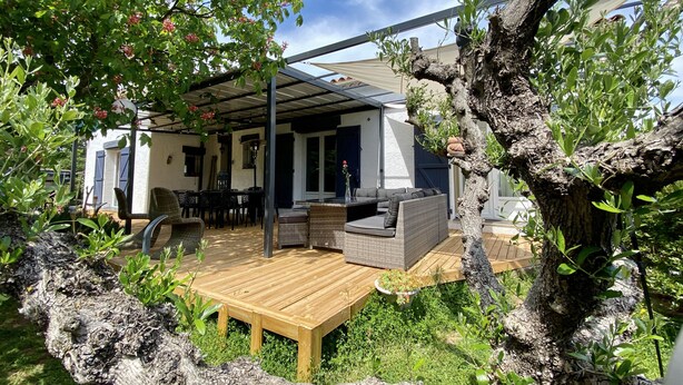 Uma área de varanda coberta com móveis de exterior, um deck de madeira e vista para o jardim circundante.
