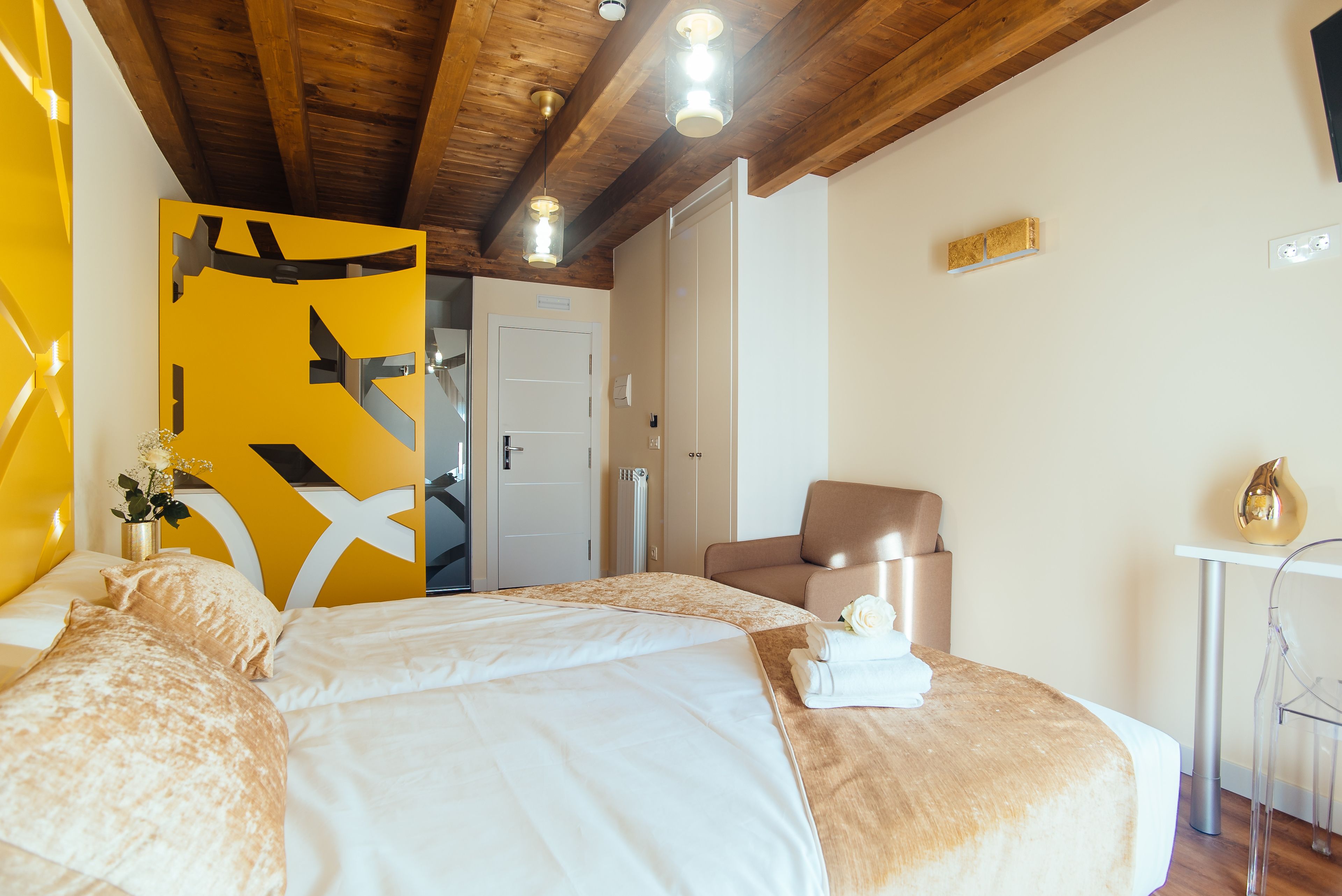 Quarto de hotel com cama, uma cadeira, escrivaninha e parede com design geométrico.