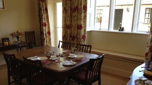 Uma sala de jantar com uma mesa de madeira posta para quatro pessoas, rodeada por cadeiras.