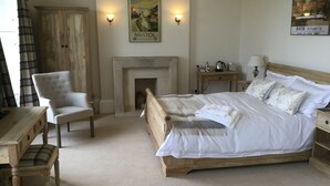 Quarto com cama grande, uma cadeira de madeira, uma mesinha, lareira e duas luminárias na parede.