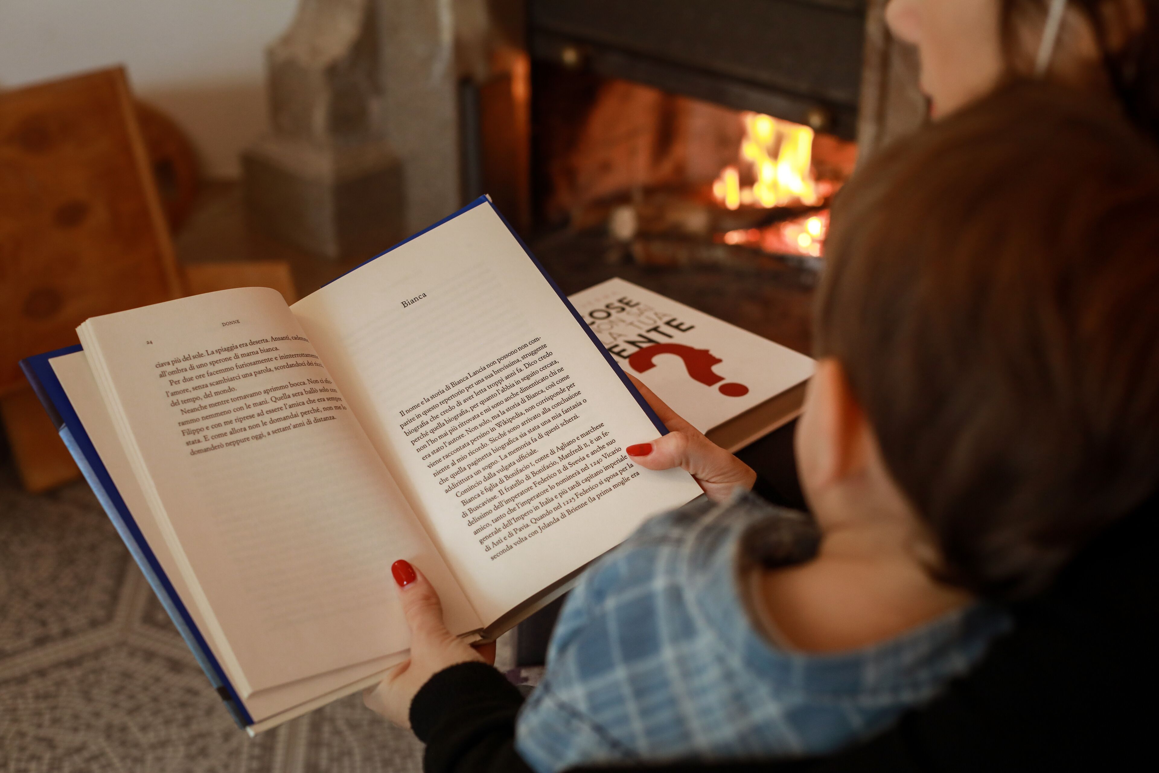 Uma pessoa lendo um livro em um quarto com lareira.