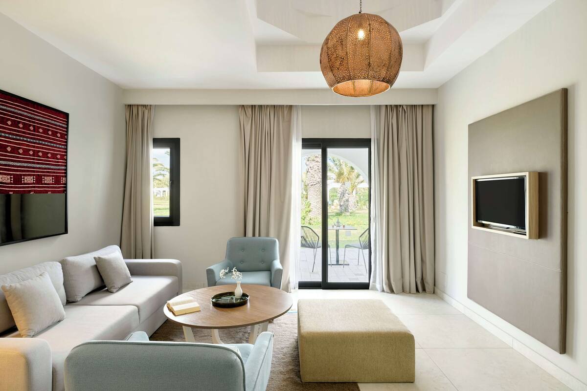 Uma sala de estar moderna com um sofá, poltronas, uma mesa de centro e uma televisão fixada na parede.