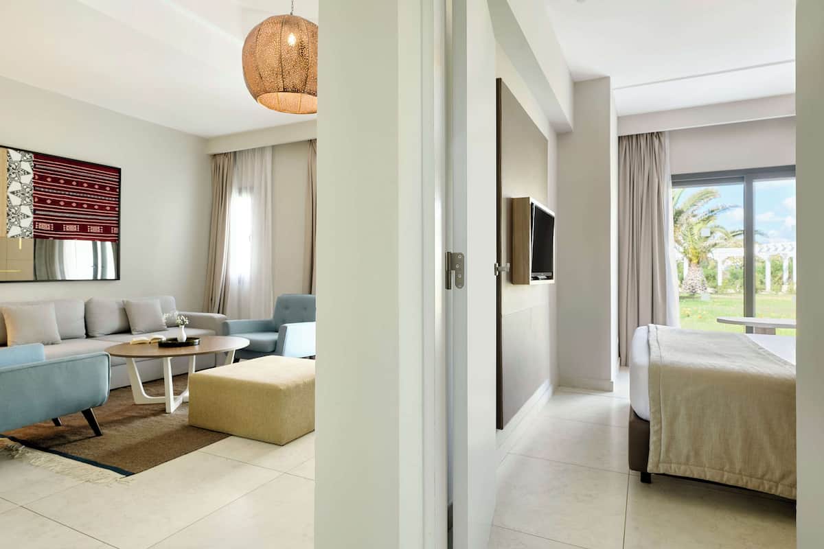 Quarto de hotel moderno com sofá, uma mesinha, cama, televisão e vista para o exterior.