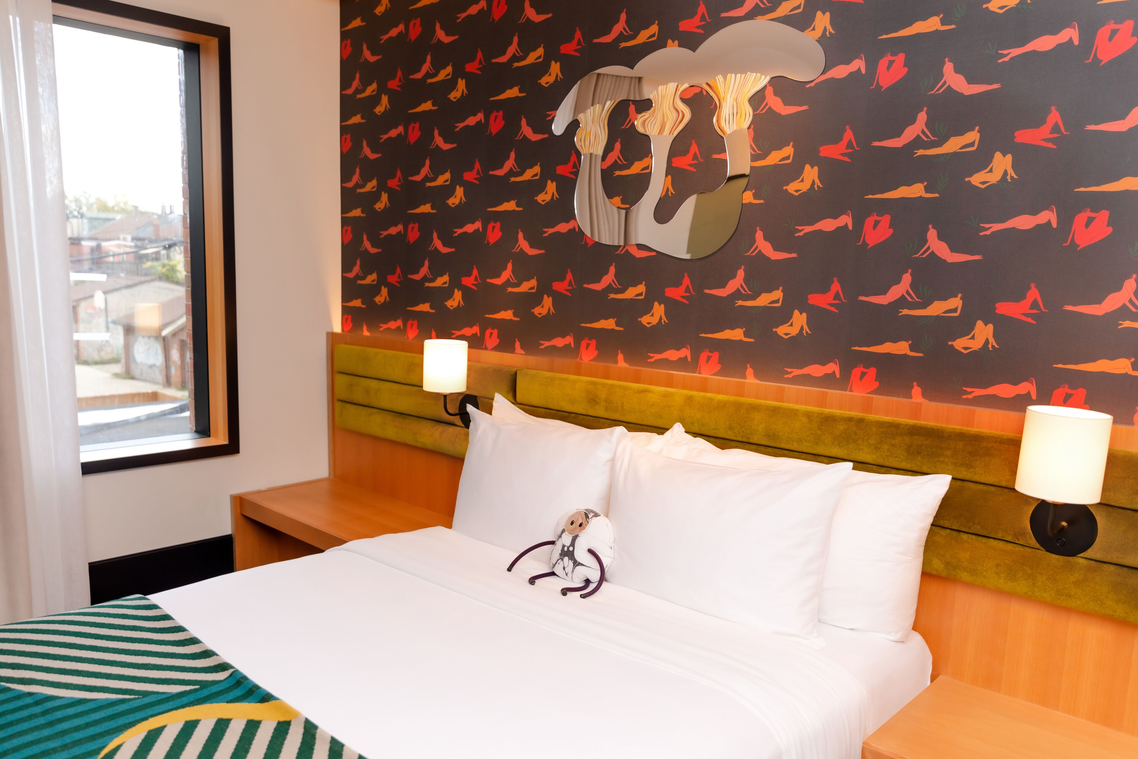 Quarto de hotel com cama, almofadas, cabeceira, decoração na parede e janela.