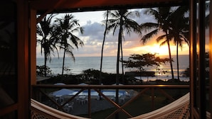 Uma rede com vista para uma área de piscina, palmeiras e um pôr do sol.