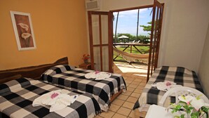 Quarto de hotel com duas camas, uma mesinha, uma cadeira e uma varanda com rede.