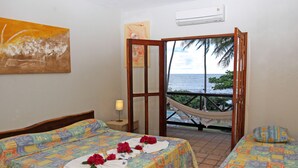 Quarto de hotel com duas camas, uma rede e varanda com vista para o mar.