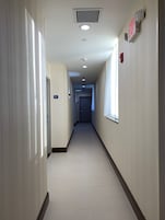 Corredor longo e estreito de hotel com placa indicando o quarto 615, um alarme de incêndio e uma saída de ventilação no teto.