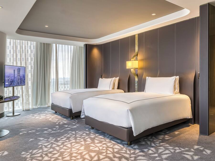 Quarto de hotel moderno com duas camas, televisão e escrivaninha.