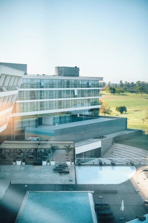 Um hotel moderno com piscina no terraço, vários andares e vista para um parque.