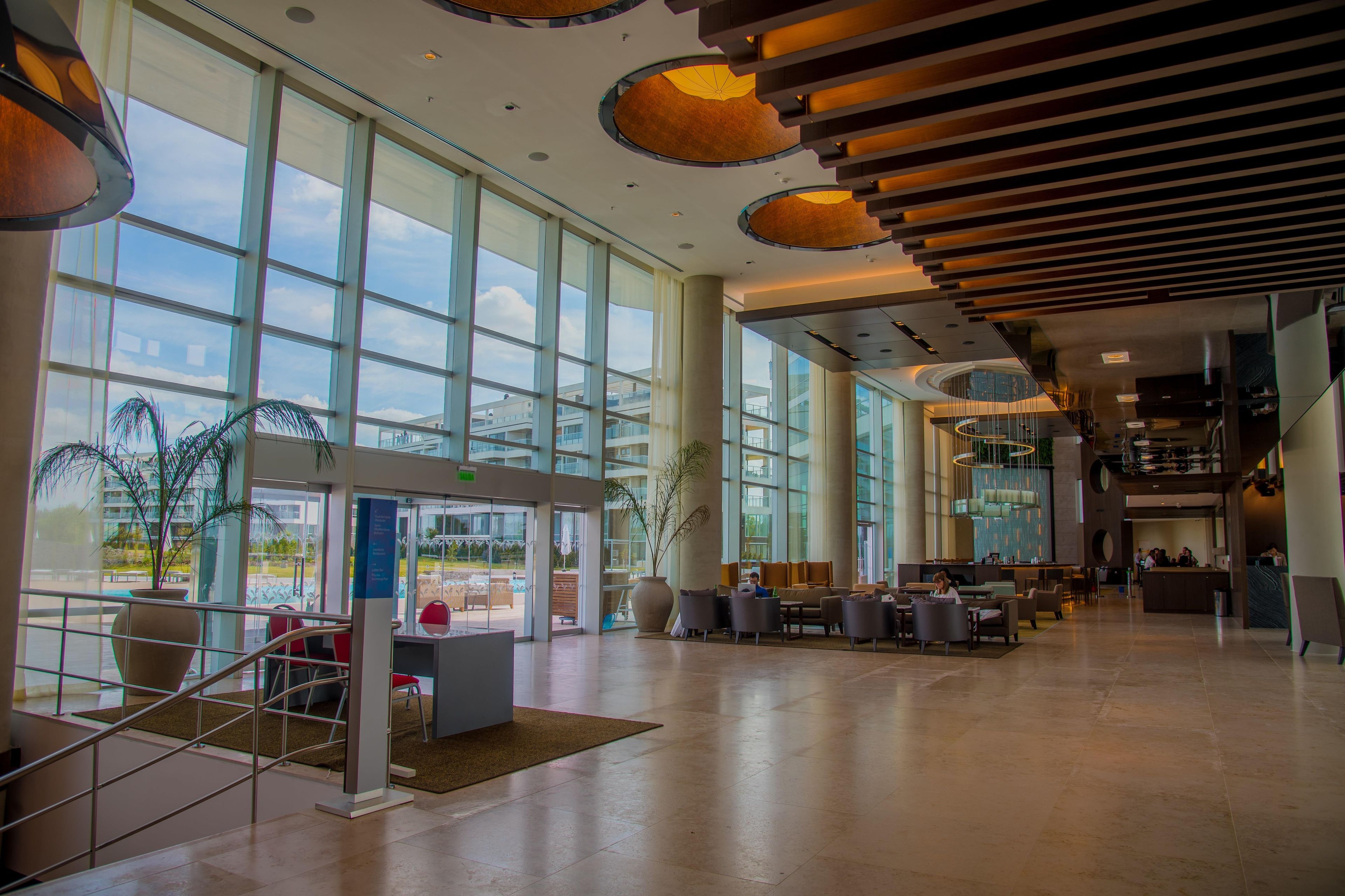 Um hall amplo com grandes janelas, balcão de recepção e luminárias modernas.