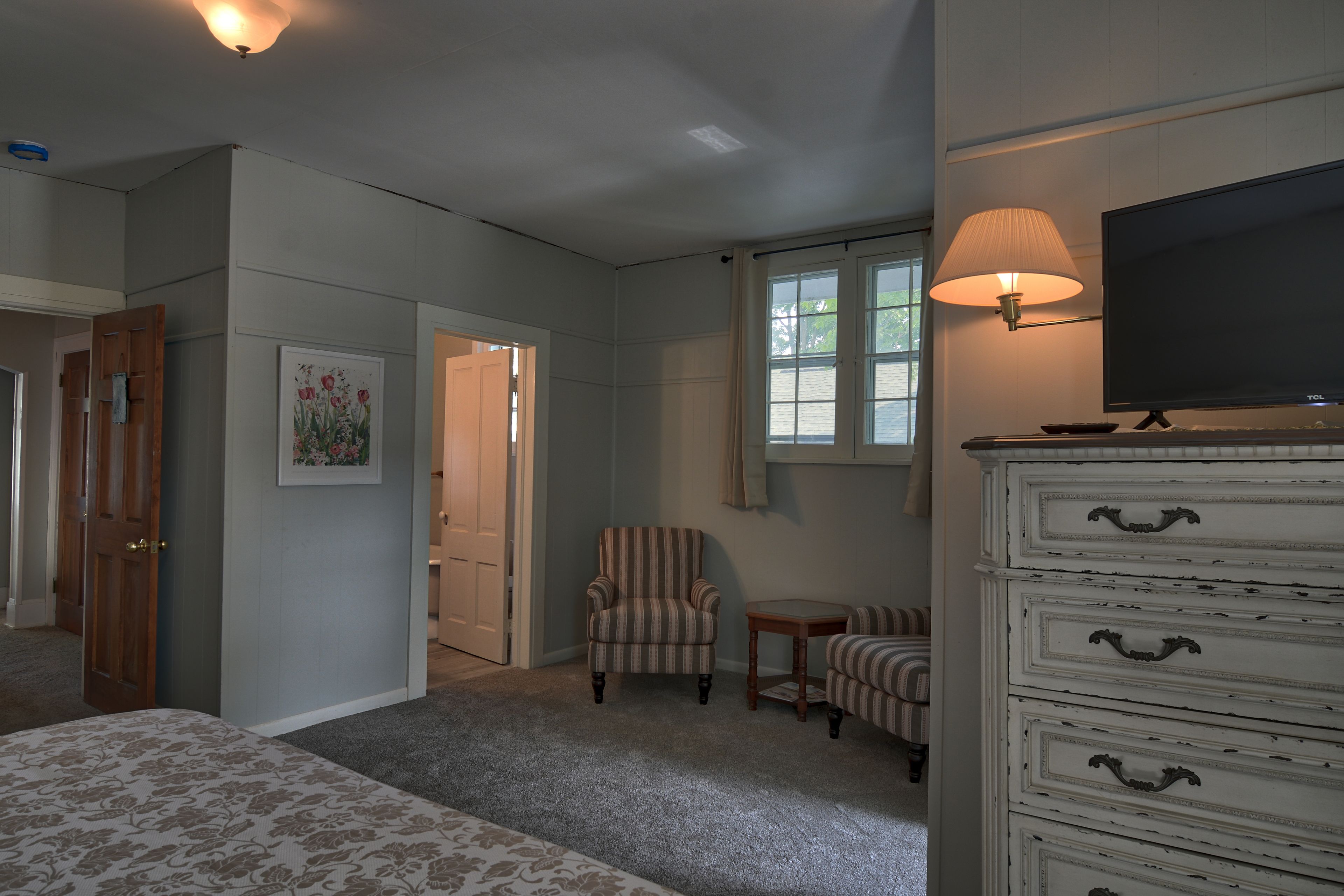 Um quarto com uma cama, cômoda, cadeira, luminária e televisão.