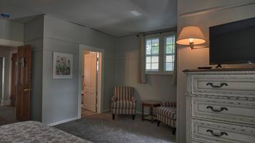 Um quarto com uma cama, cômoda, cadeira, luminária e televisão.
