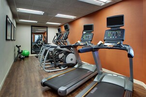 Uma academia com esteiras, elípticos e uma bola de exercício verde.