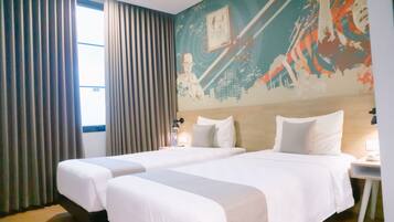 Quarto de hotel com duas camas, uma janela grande com cortinas, um mural na parede e uma mesa de cabeceira com abajur.