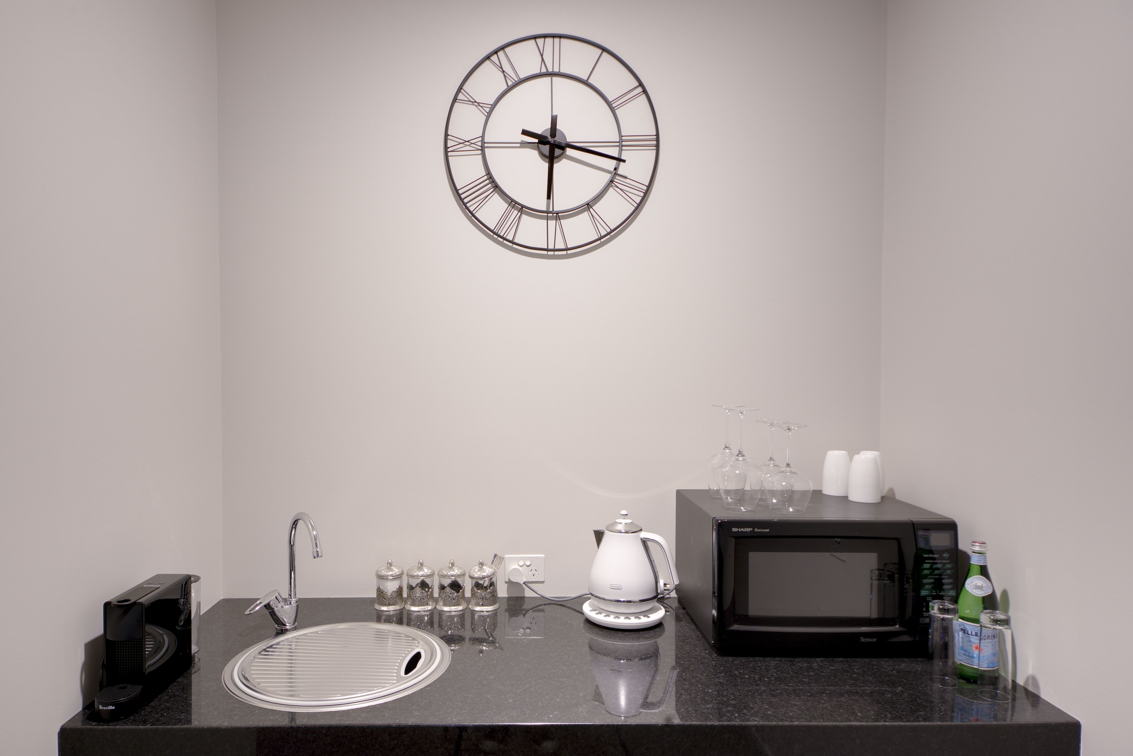 Cozinha equipada com relógio, máquina de café, micro-ondas e copos de vinho.