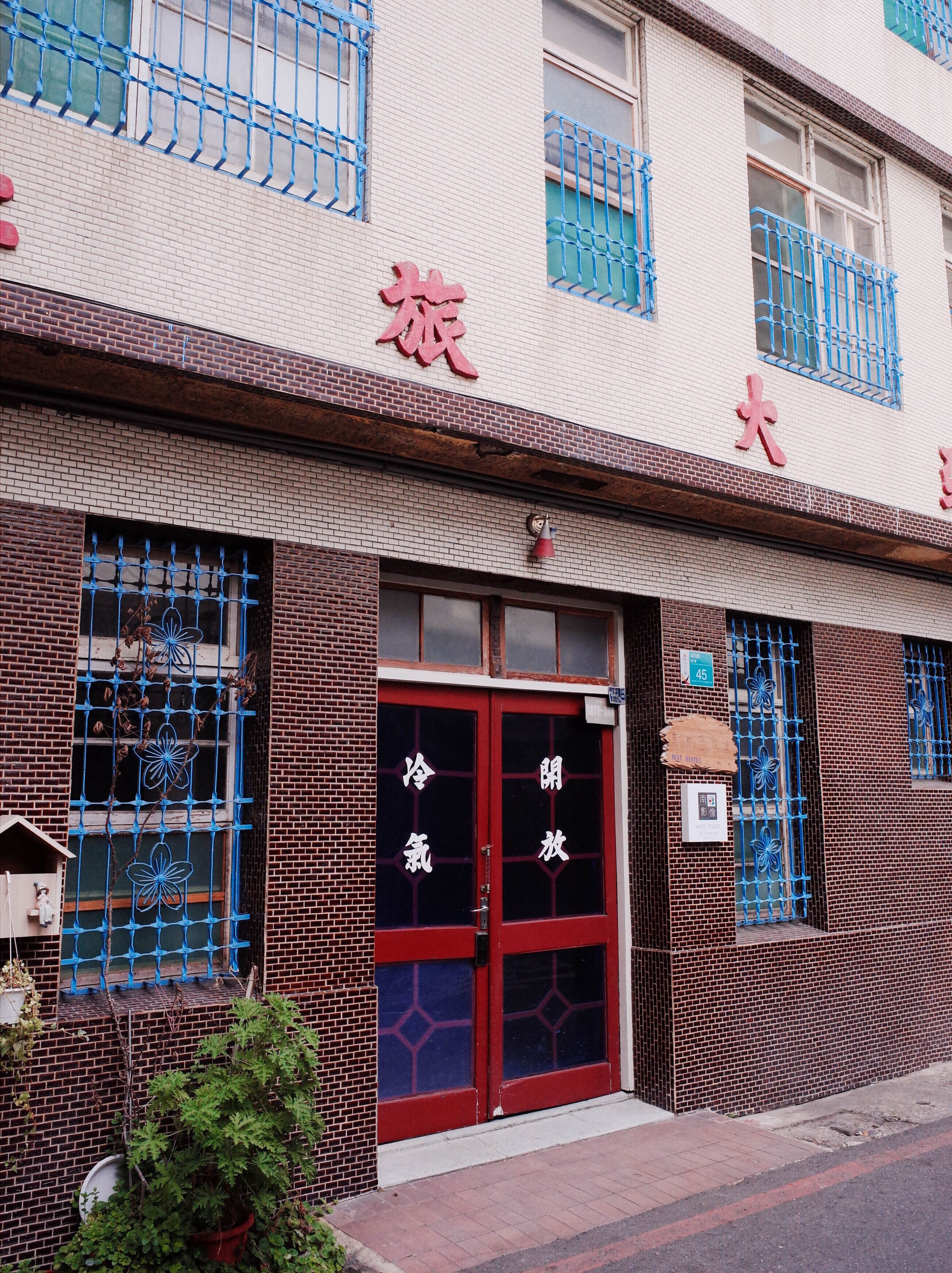 Um edifício com porta vermelha e grades azuis nas janelas, apresentando caracteres chineses e uma placa com o número 45.