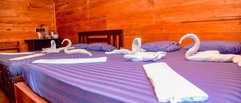 Quarto de cabana de madeira com duas camas, cada uma com roupa de cama roxa e toalhas brancas dispostas em formato de cisne.