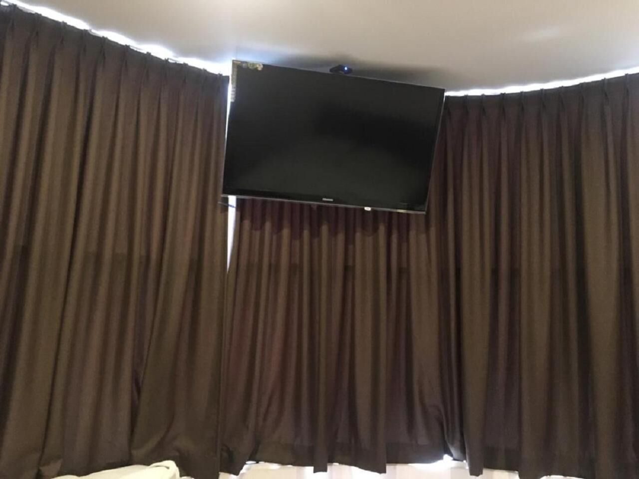 Quarto com uma grande televisão de tela plana fixada na parede, rodeado por cortinas escuras.