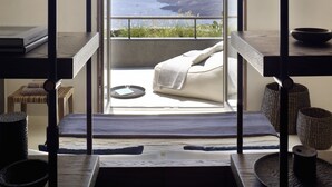 Quarto com vista para o mar, uma cama, uma mesa e uma cadeira.