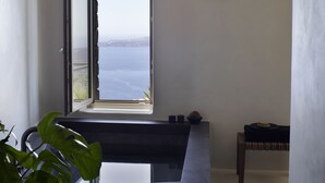 Um banheiro moderno com uma banheira grande, uma janela com vista para o mar e um pequeno banco de madeira.