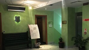 Um hall com parede verde, um banco de madeira, um mural de avisos e plantas em vasos.