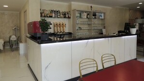 Cozinha com bancada de mármore, mesa vermelha e cadeiras. Há prateleiras com garrafas e copos.