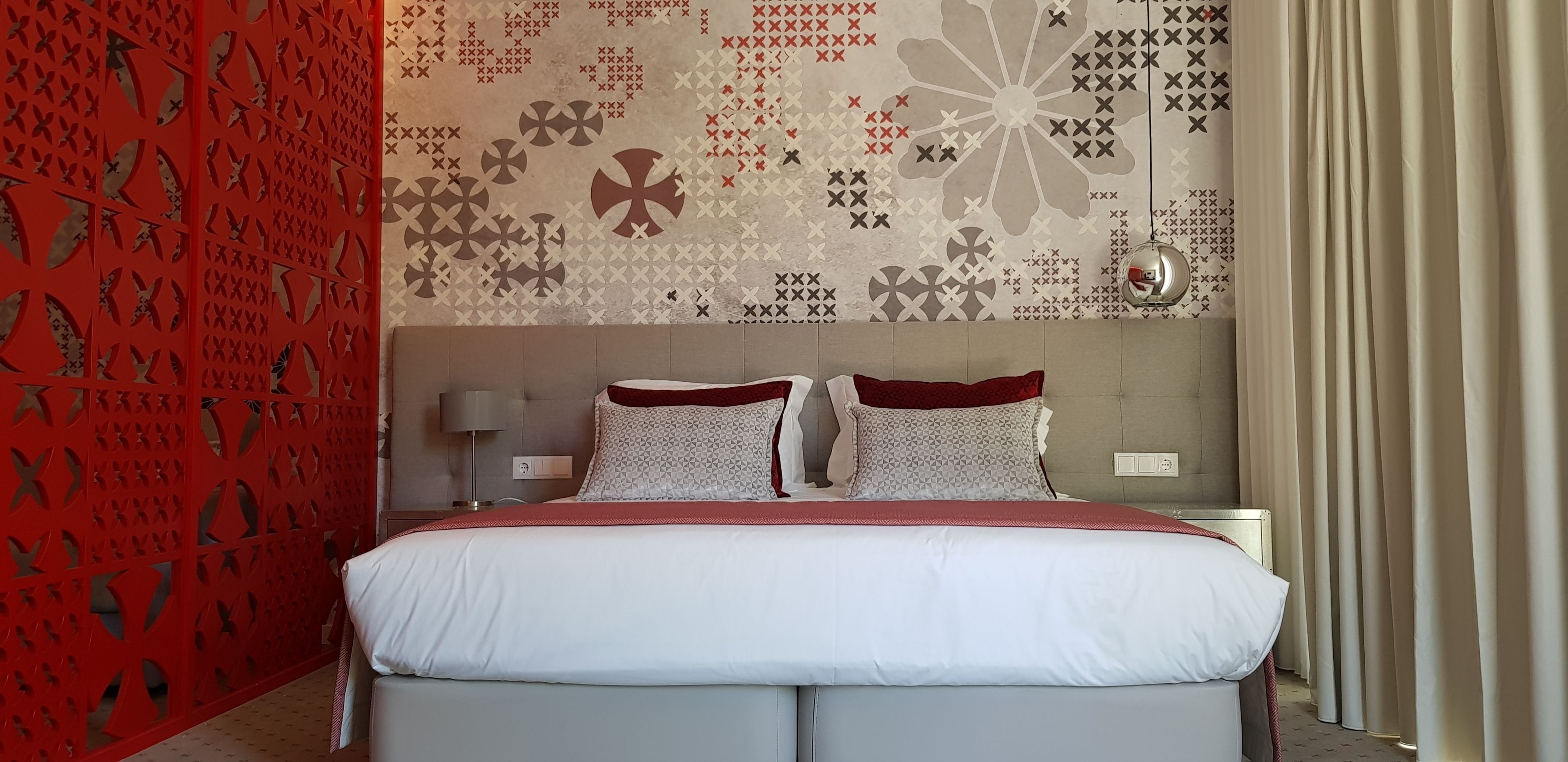 Quarto de hotel com cama, mesa de cabeceira, abajur e parede estampada.