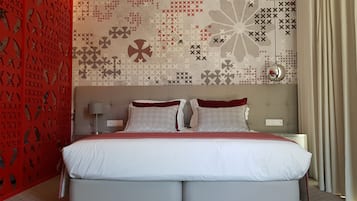 Quarto de hotel com cama, mesa de cabeceira, abajur e parede estampada.