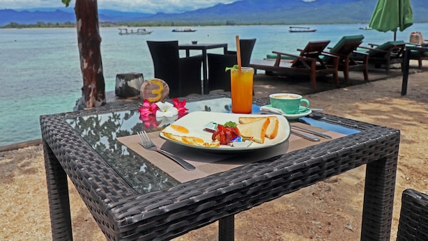 Uma mesa de jantar com um prato de comida, uma bebida e uma chávena, com vista para um corpo de água e montanhas.