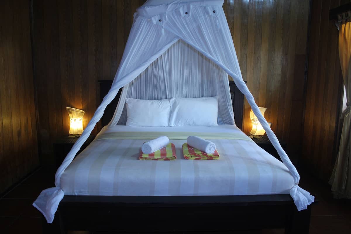 Uma cama com dossel, duas luminárias de cabeceira e duas toalhas enroladas sobre a cama.