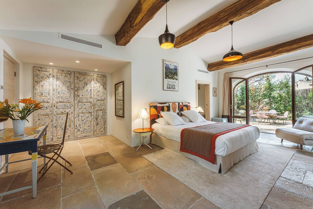 Quarto com cama, mesas de cabeceira, uma cadeira e vista para o exterior.