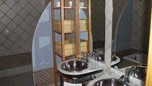 Casa de banho com um espelho grande, duas bacias e uma prateleira de madeira com cestos.