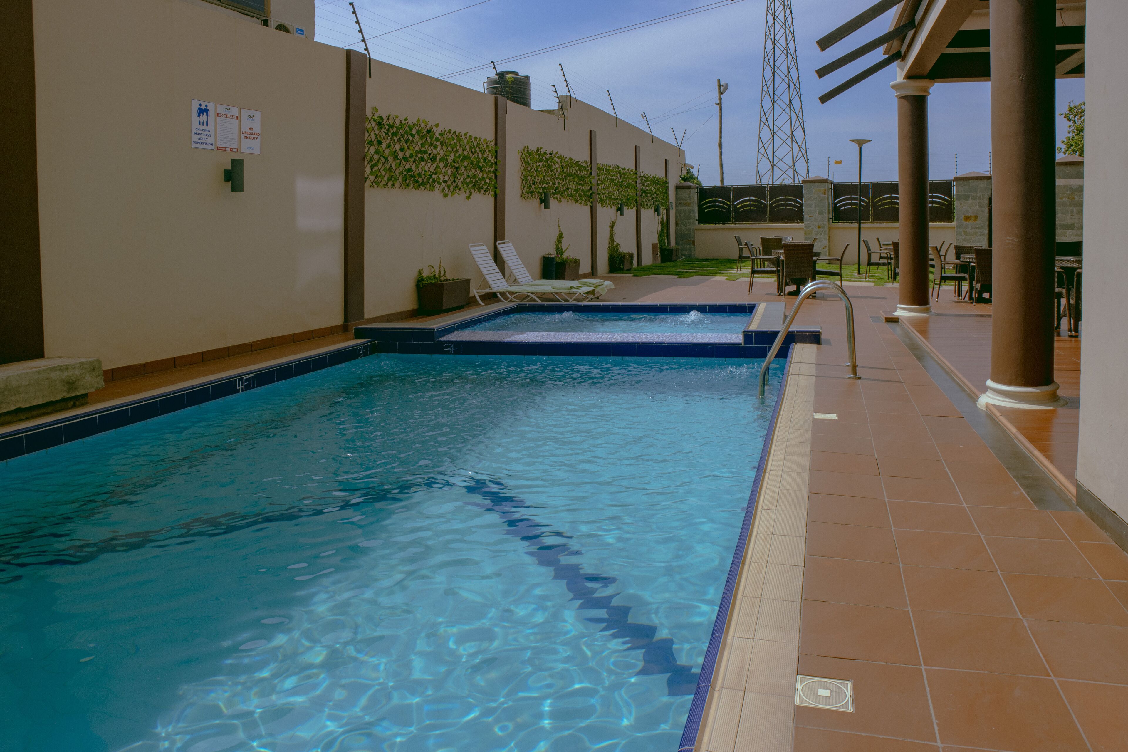 Uma piscina com água cristalina, rodeada por um deck revestido, espreguiçadeiras e uma estrutura de pérgula.