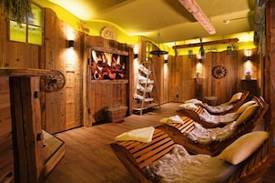 Um spa com sala de madeira, lareira, bancos de madeira e plantas penduradas.