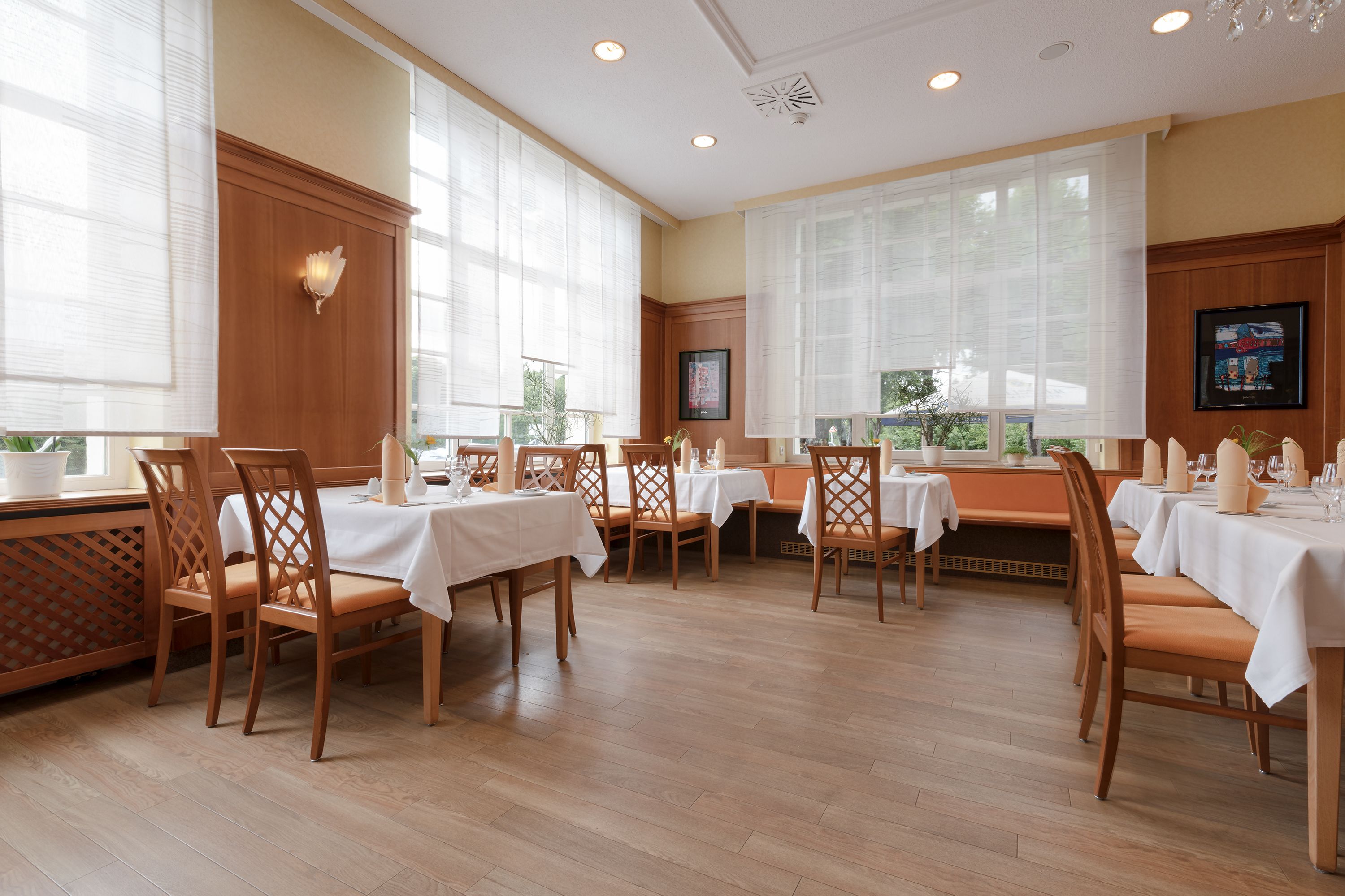 Um restaurante com pisos de madeira, toalhas de mesa brancas e cadeiras de madeira.
